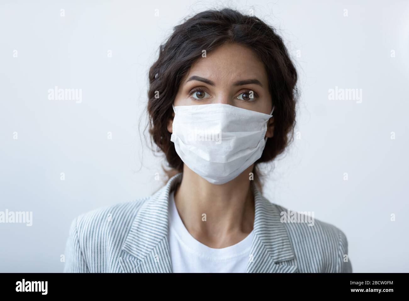 Worrying young brunette woman covering nose and mouth with medical mask ...