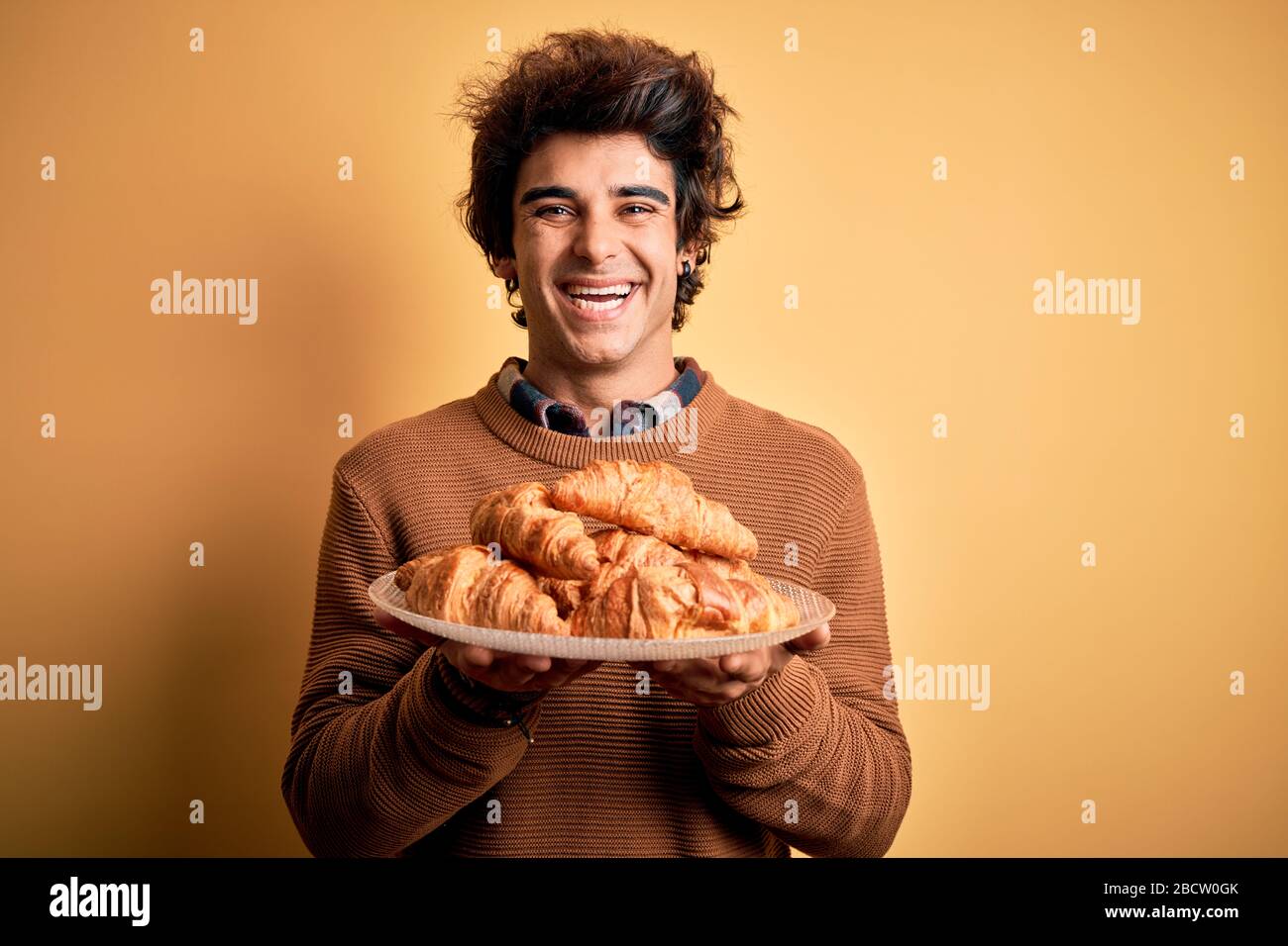 Young handsome man holding plate with croissants standing over isolated ...