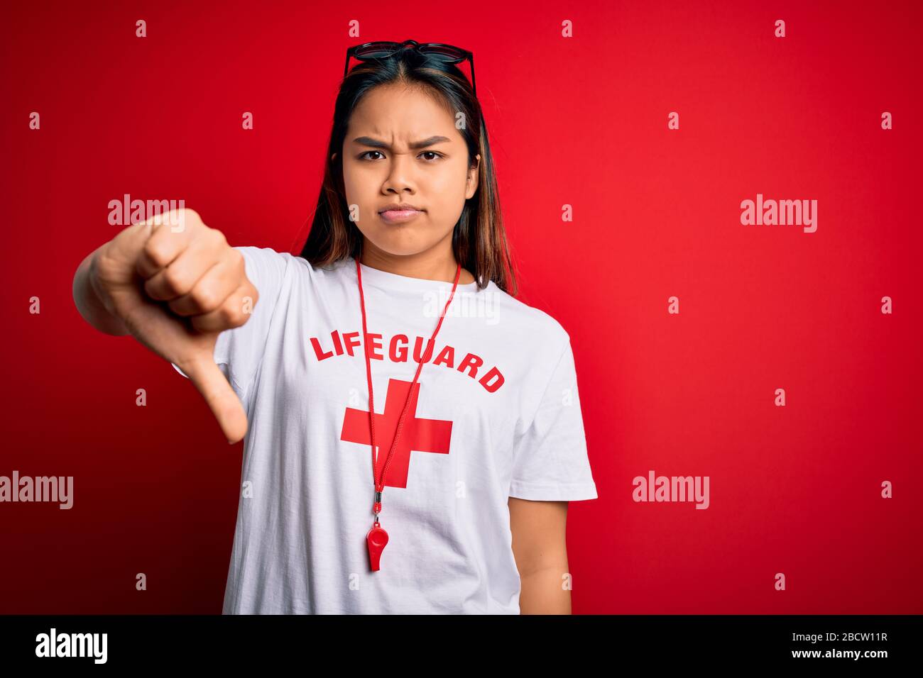 Young asian lifeguard girl wearing t-shirt with red cross using whistle ...
