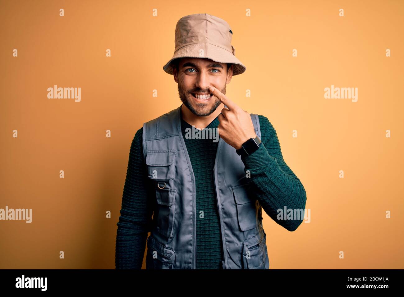 Handsome tourist man with beard on vacation wearing explorer hat over ...