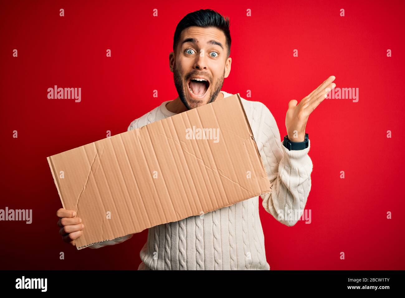 Young handsome man holding blank cardboard banner over isolated red ...