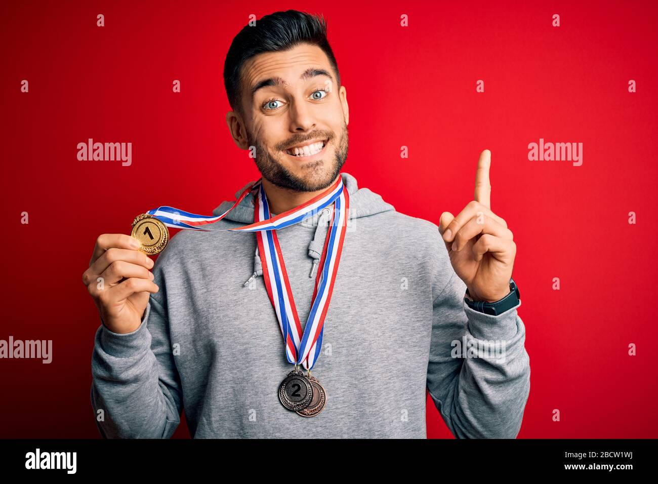 Young handsome succesful man winning medals standing over isolated red ...