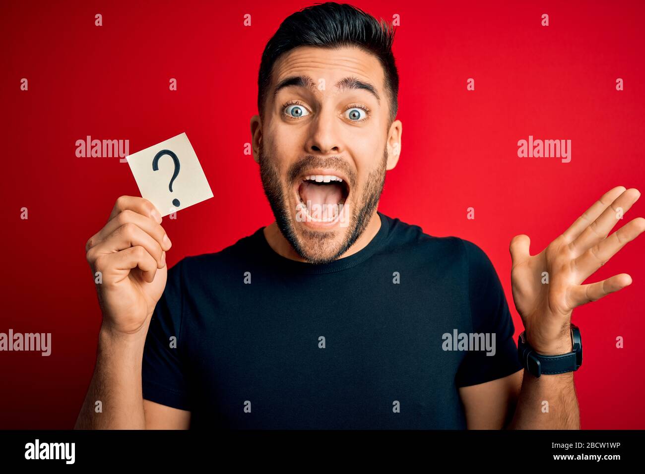 Young handsome man holding paper with question mark symbol over red ...