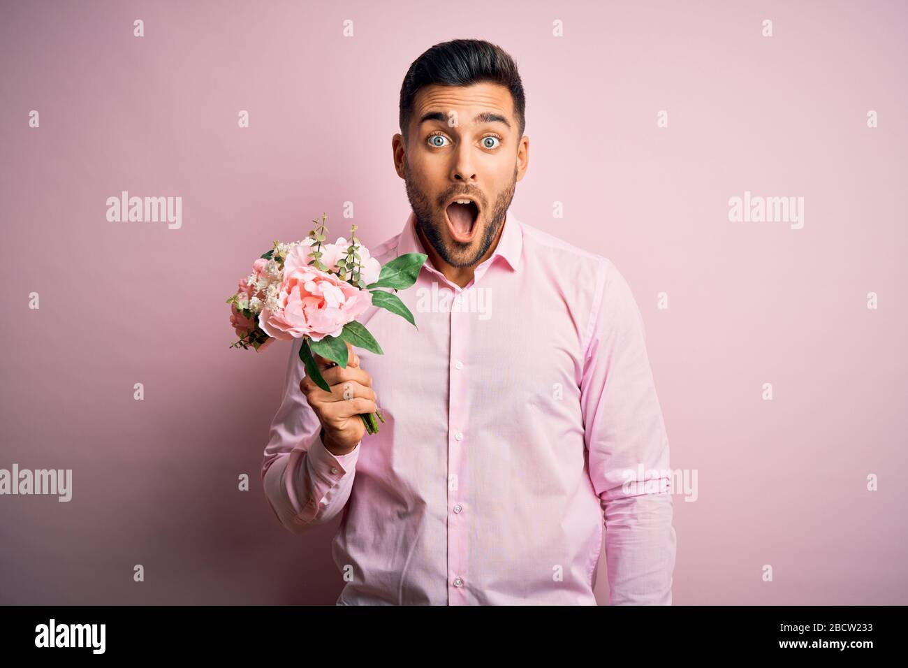 Young romatic man holding bouquet of spring flowers over pink isolatd ...