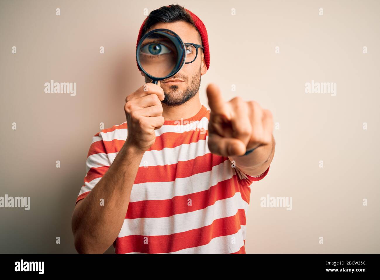 Young detective man looking through magnifying glass over isolated ...