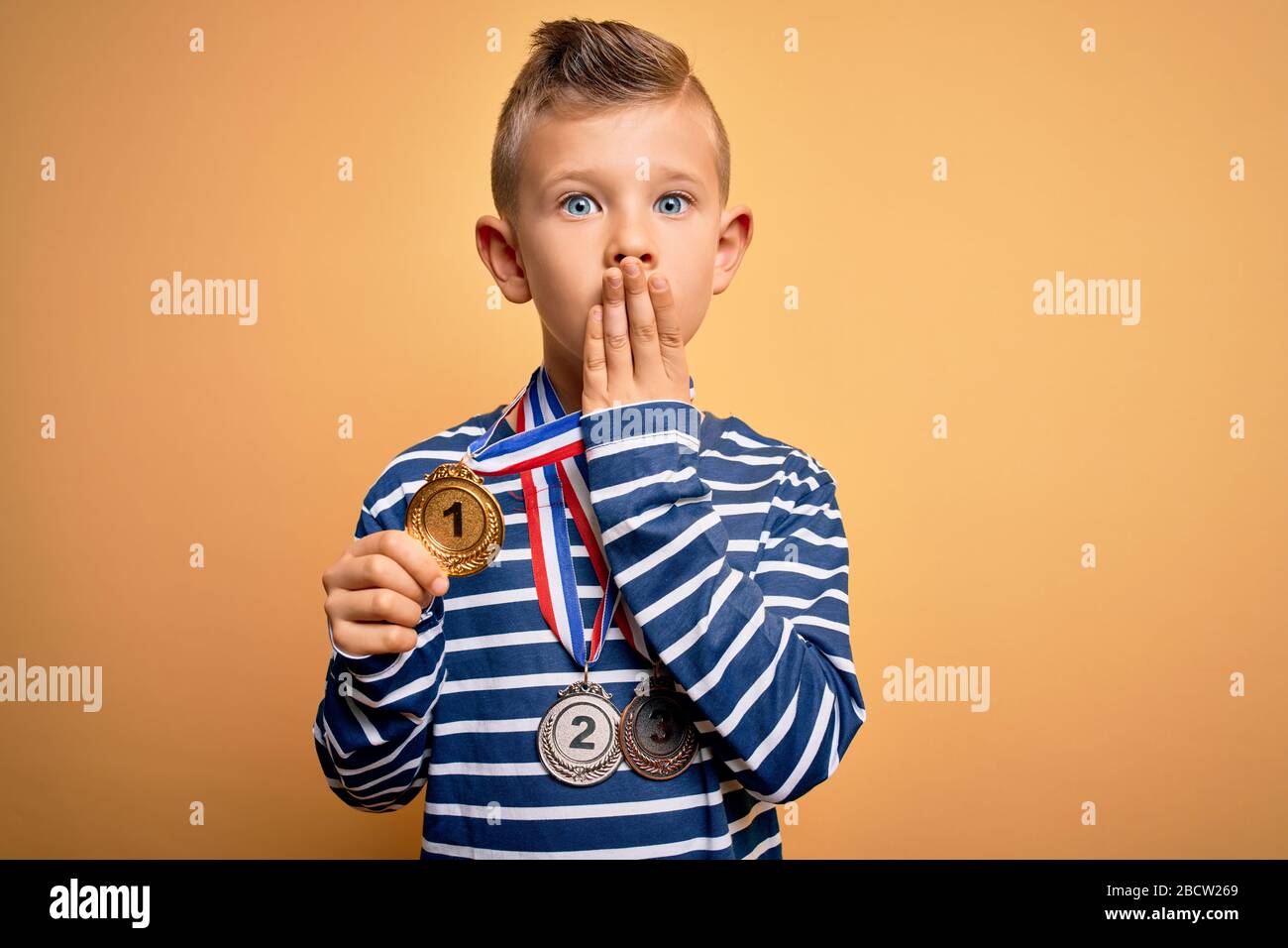 Young little caucasian winner kid wearing award competition medals over ...