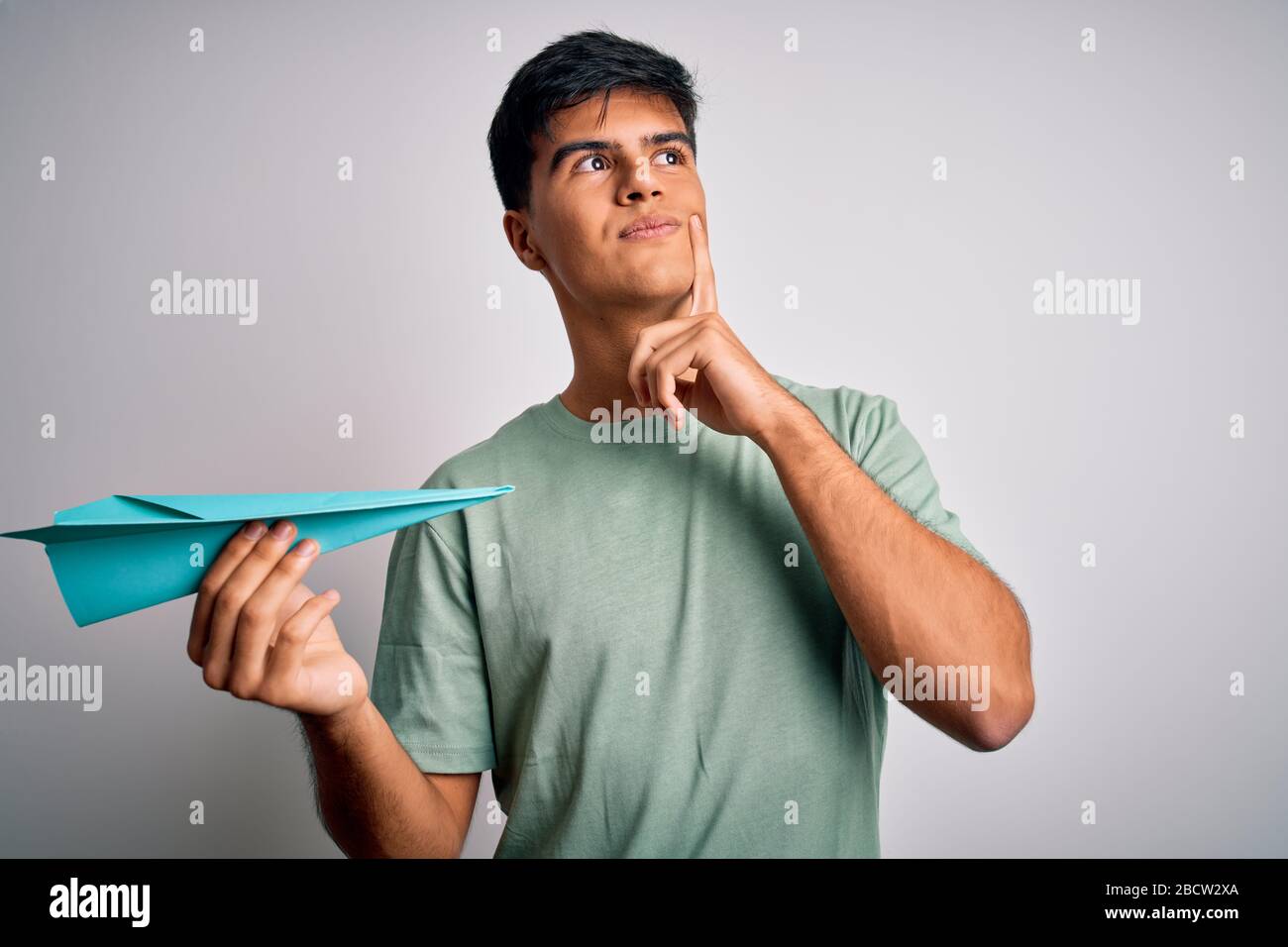 Young handsome man holding paper airplane over isolated white ...