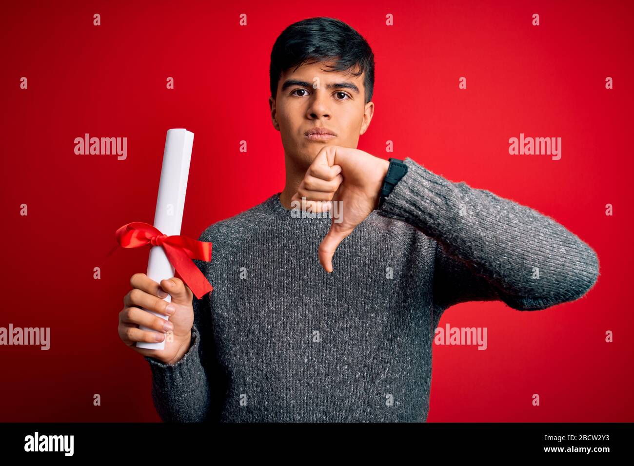 Young student man holding university graduated diploma degree over red ...
