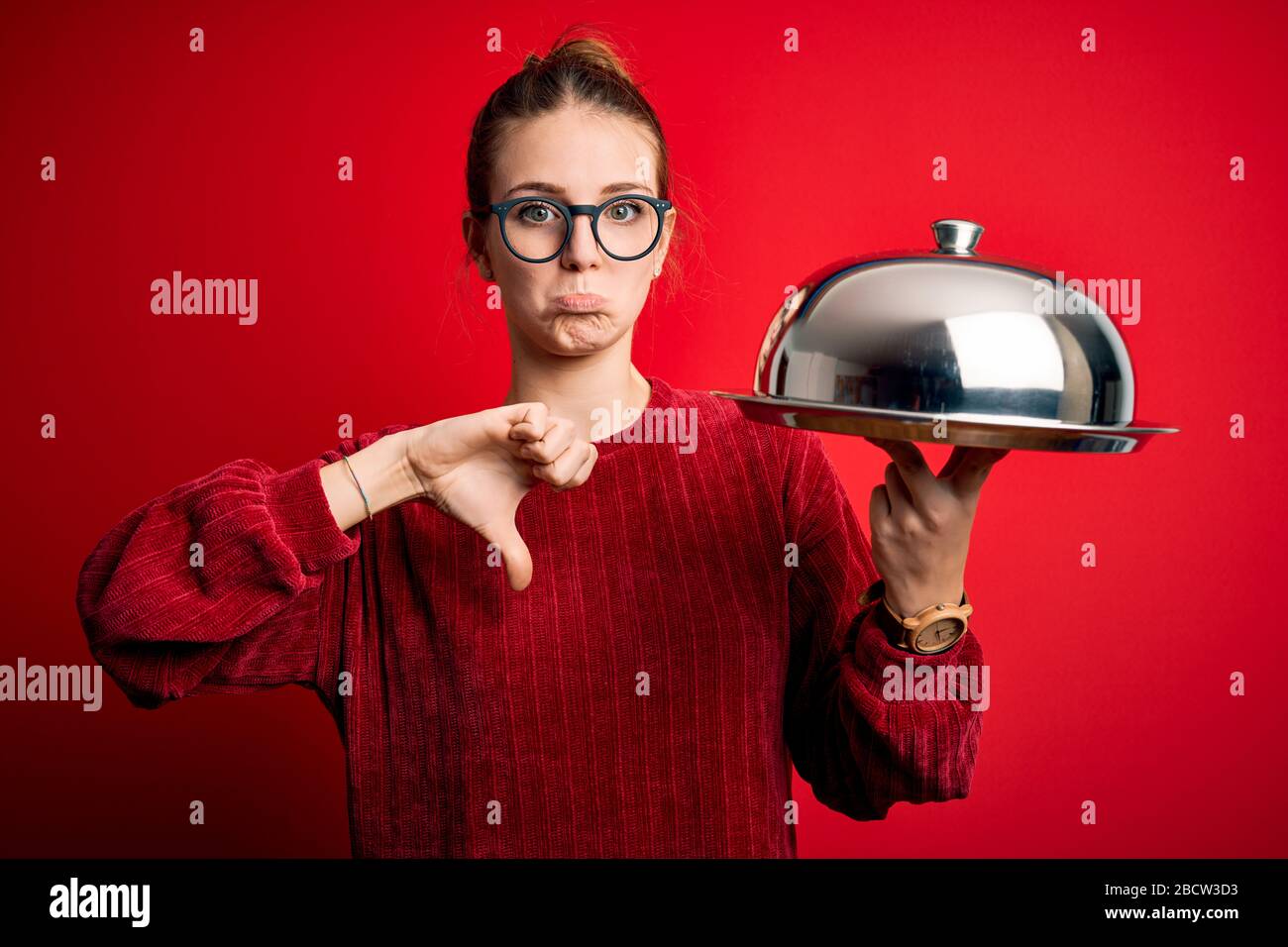 Young beautiful redhead woman holding waitress tray over isolated red ...