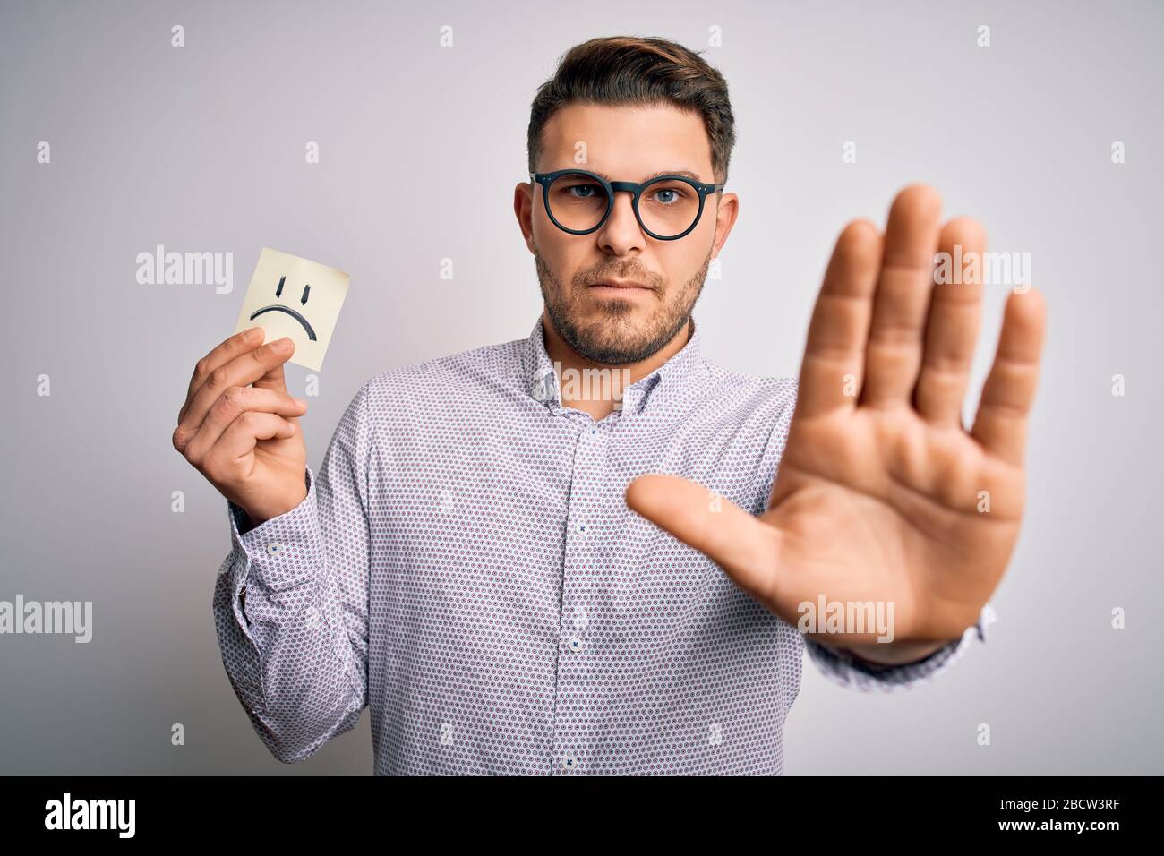 Young business man with blue eyes holding paper note with sad face as ...