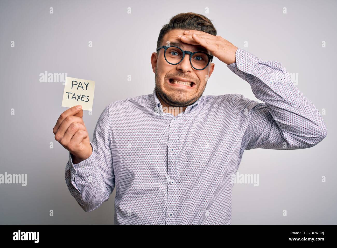 Young business man with blue eyes holding pay taxes word on paper note ...