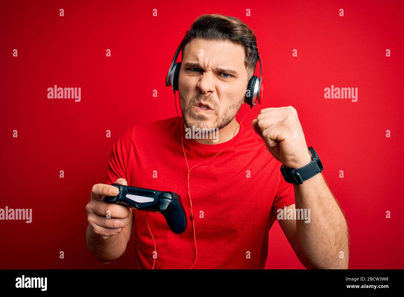Young gamer man with blue eyes playing video games using gamepad ...