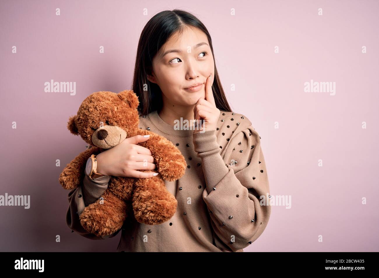 Young asian woman hugging teddy bear stuffed animal over pink isolated ...