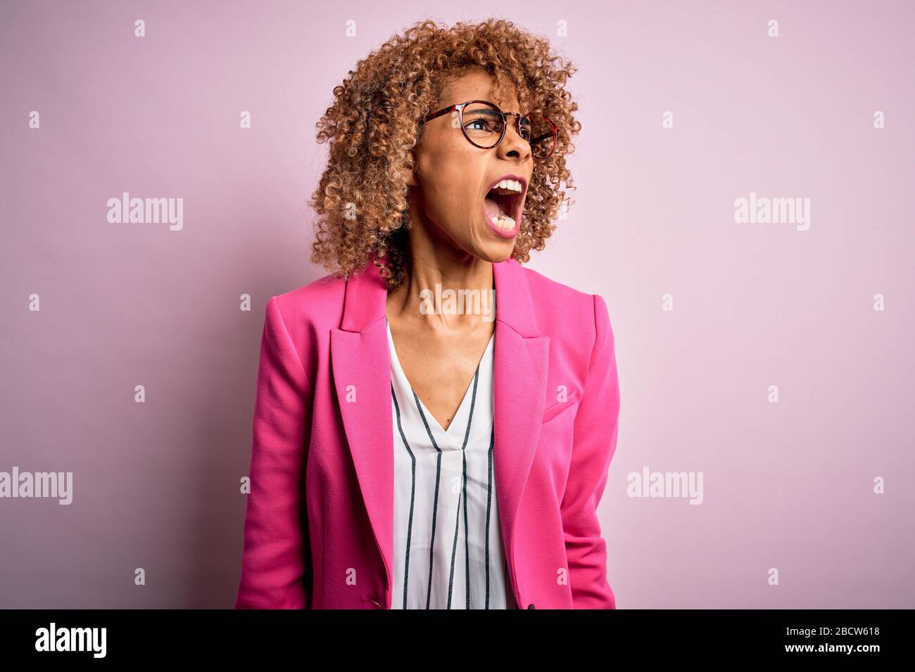Young african american businesswoman wearing glasses standing over pink ...