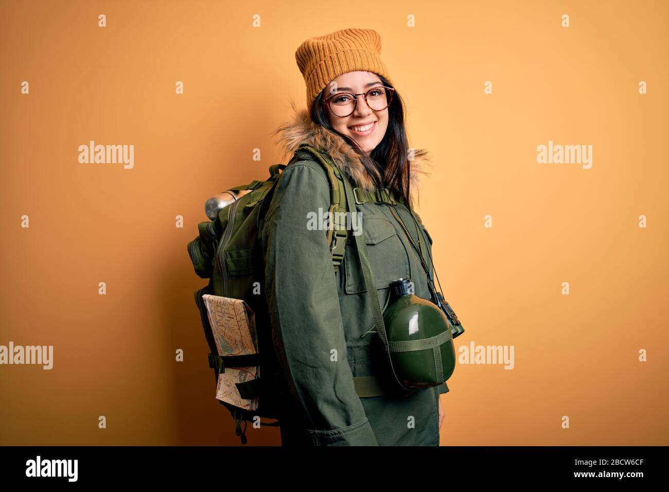 Young hiker woman wearing hiking backpack, canteen and map over yellow ...