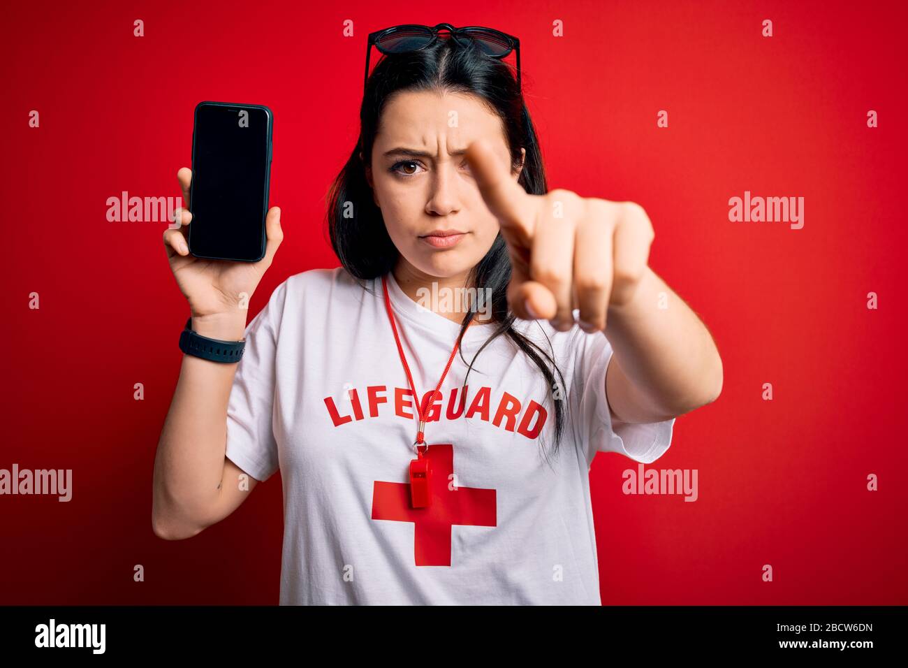 Young lifeguard woman showing smartphone screen over red background ...