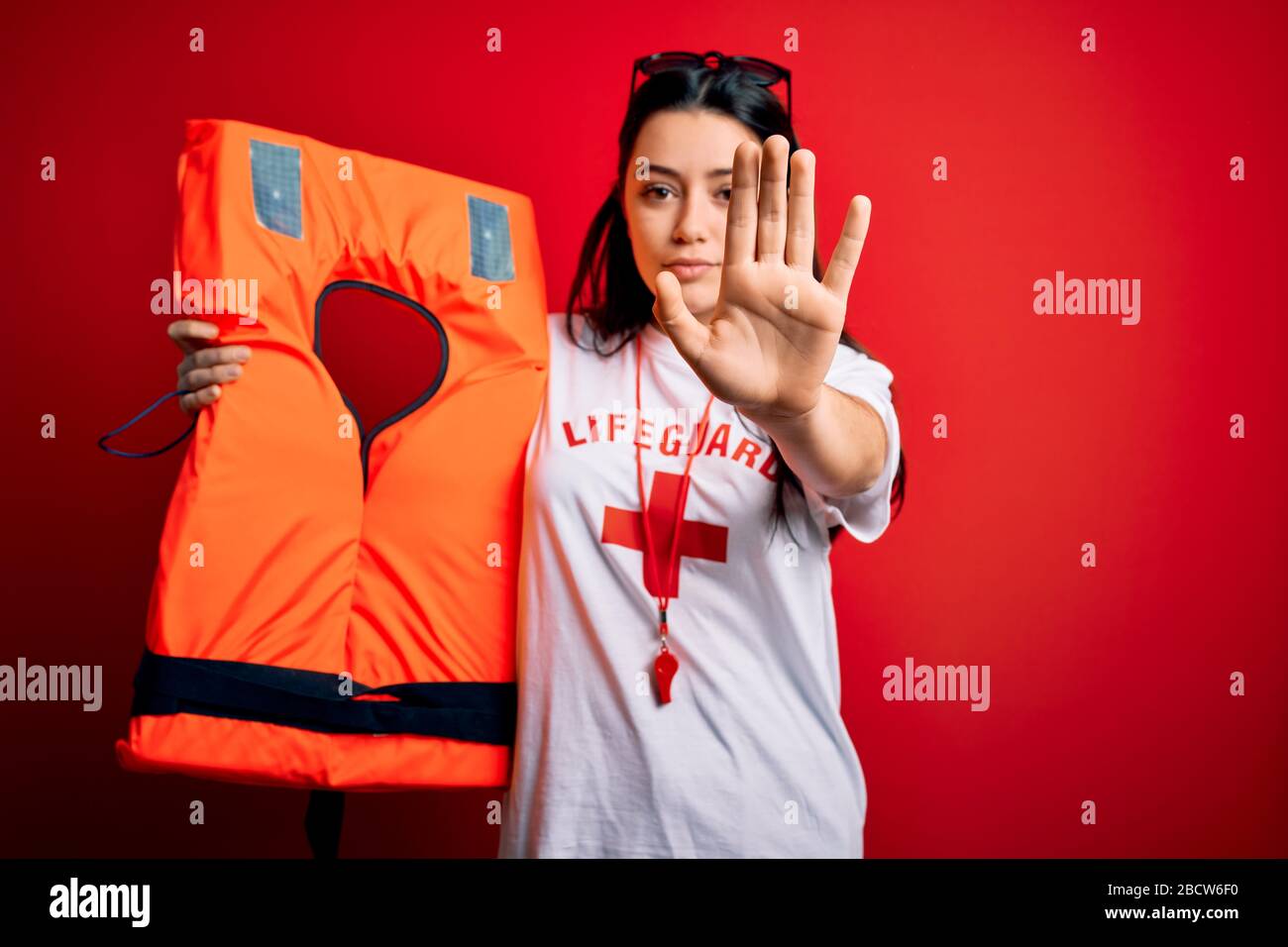 Young lifeguard woman holding rescue lifejacket over red background ...
