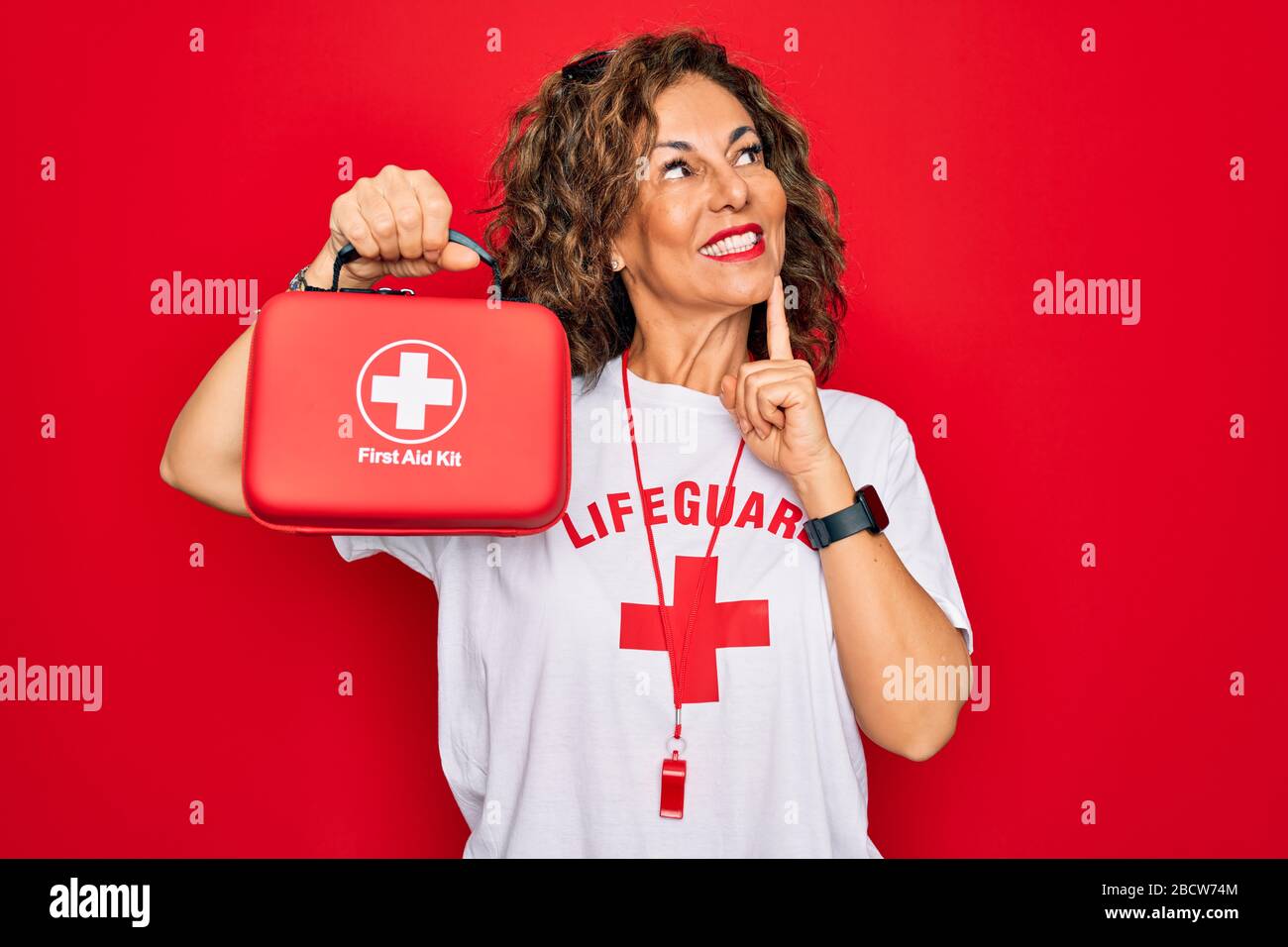Middle age senior summer lifeguard woman holding first aid kit over red ...
