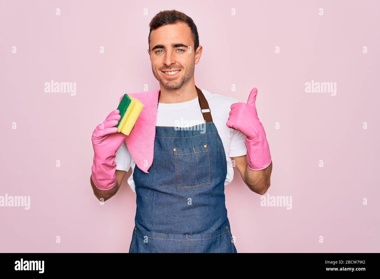 Young cleaner man with blue eyes cleaning wearing apron and gloves ...