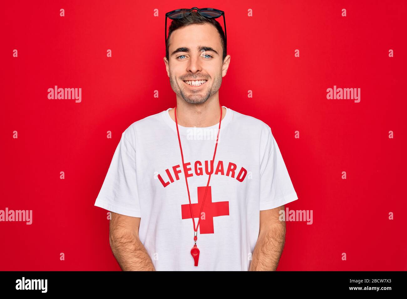 Handsome lifeguard man wearing t-shirt with red cross and whistle over ...
