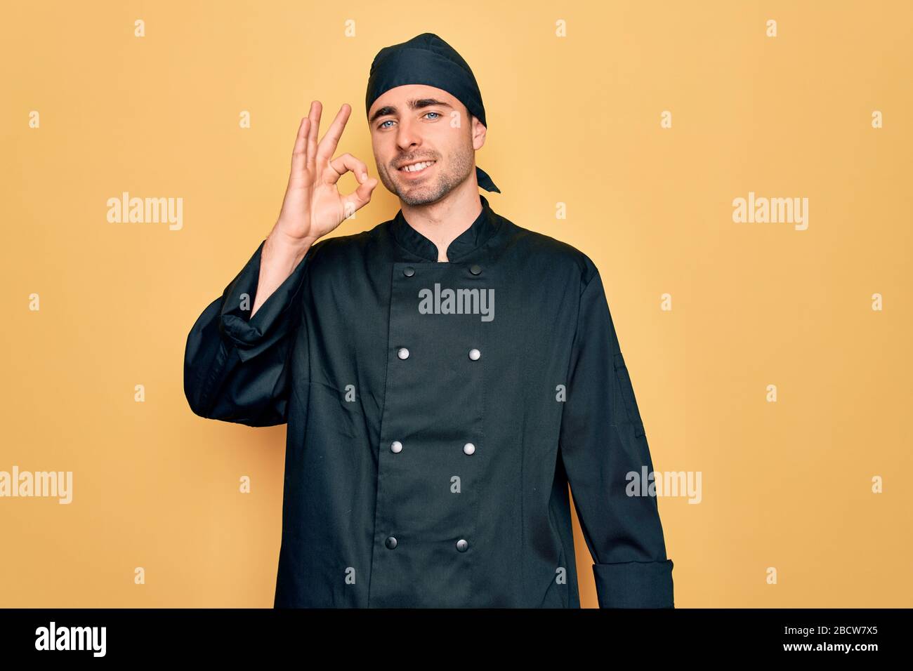 Young handsome cooker man with blue eyes wearing uniform and hat over ...