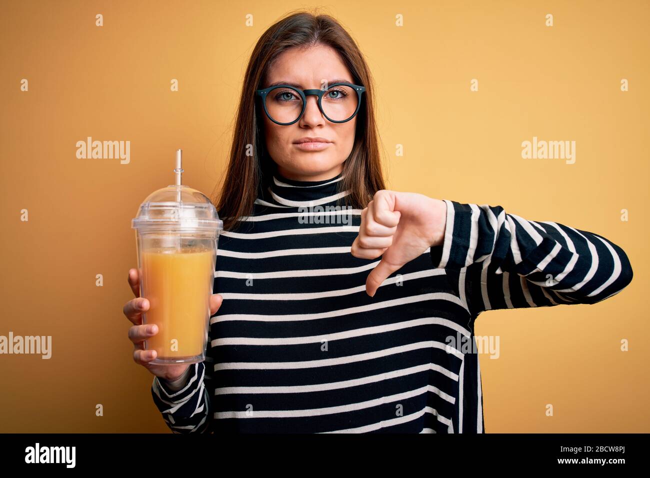 Young beautiful woman with blue eyes drinking healthy orange juice over ...
