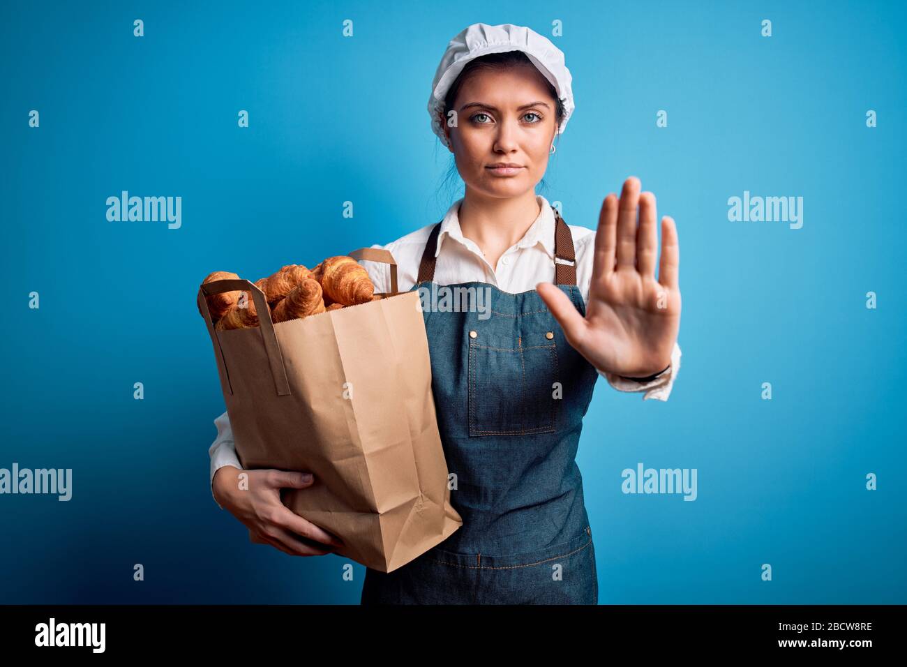 Young beautiful baker woman with blue eyes wearing apron holding paper ...