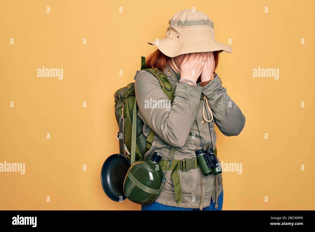 Young redhead backpacker woman hiking wearing backpack and hat over ...
