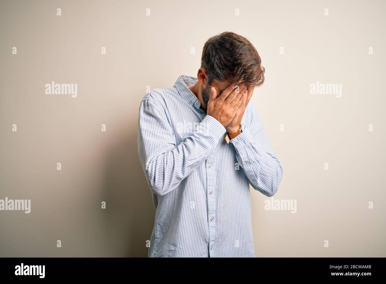 Young handsome man with beard wearing striped shirt standing over white ...