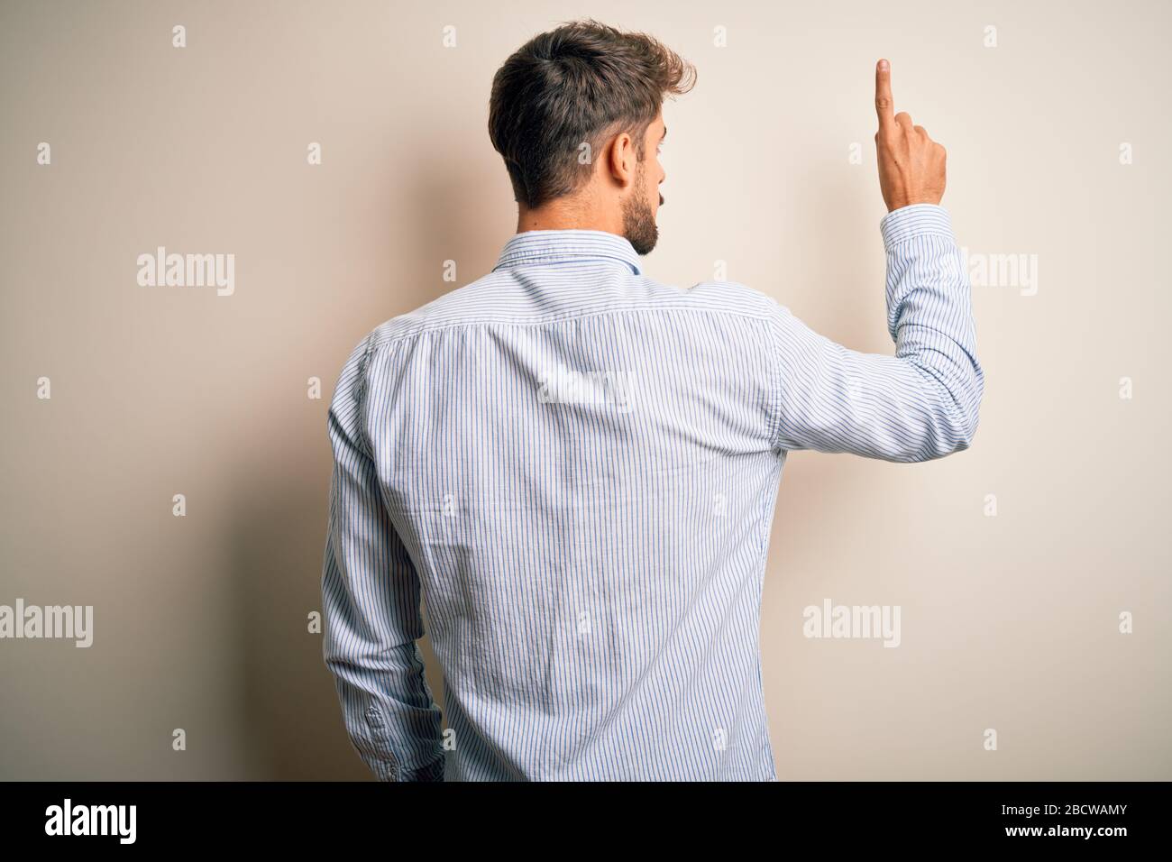 Young handsome man with beard wearing striped shirt standing over white ...