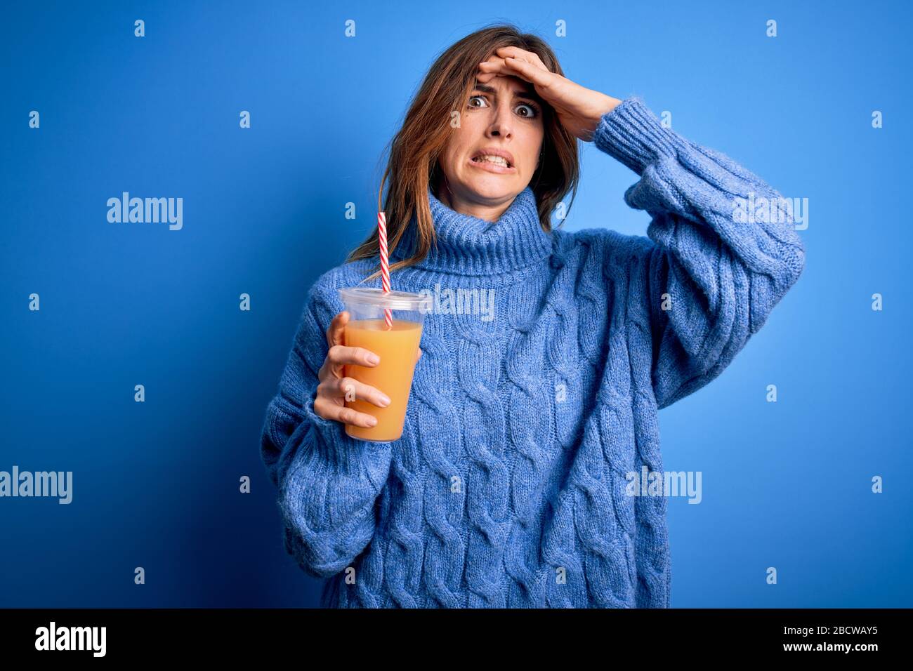 Young beautiful brunette woman drinking healthy orange juice over blue ...