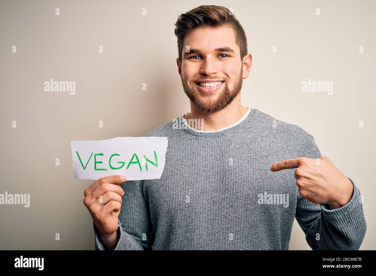 Young blond veggie man with beard and blue eyes holding paper with ...
