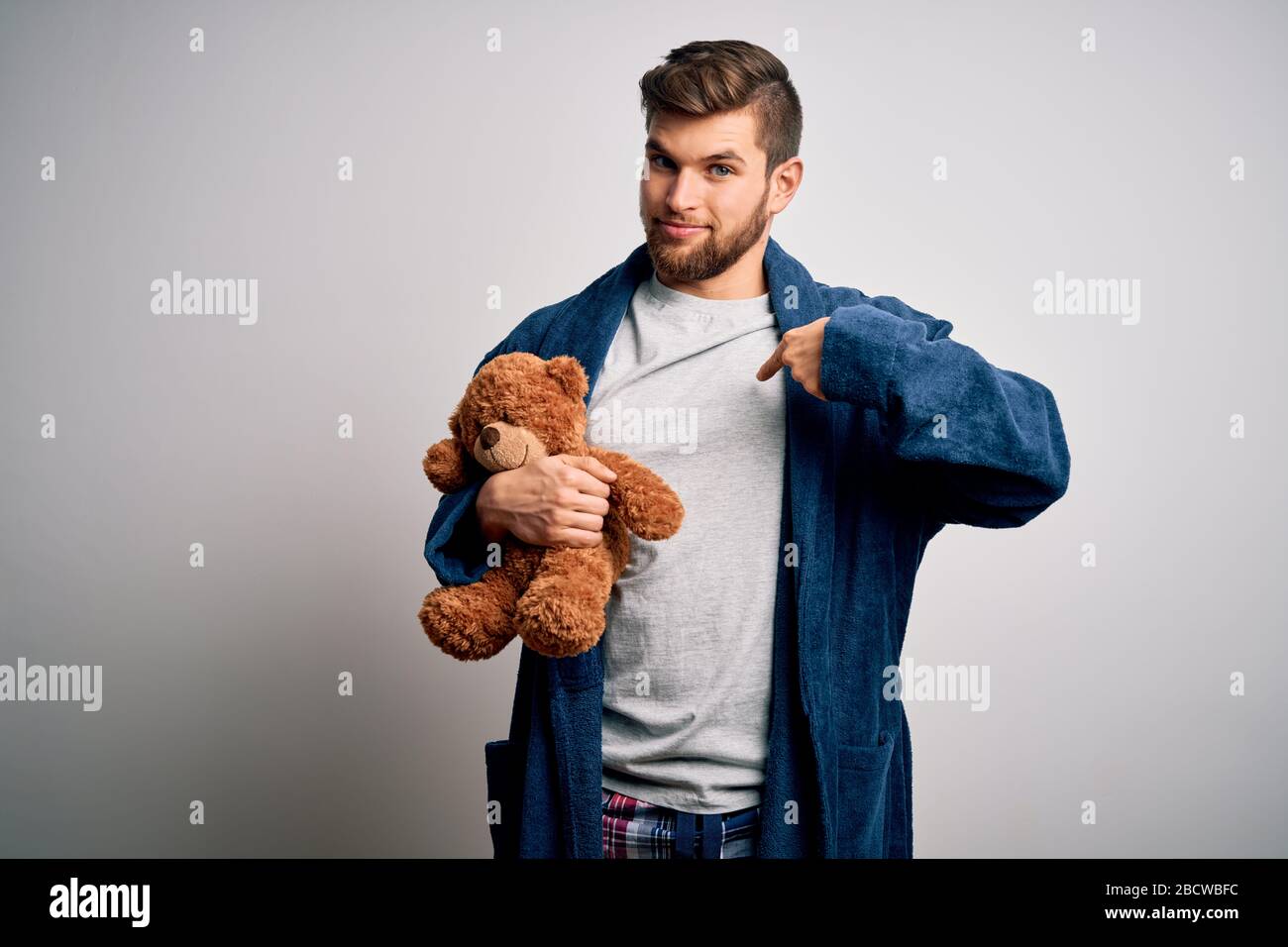 Young blond man with beard and blue eyes wearing pajama holding teddy ...