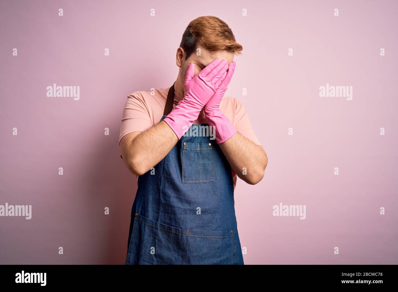 Young handsome redhead cleaner man doing housework wearing apron and ...