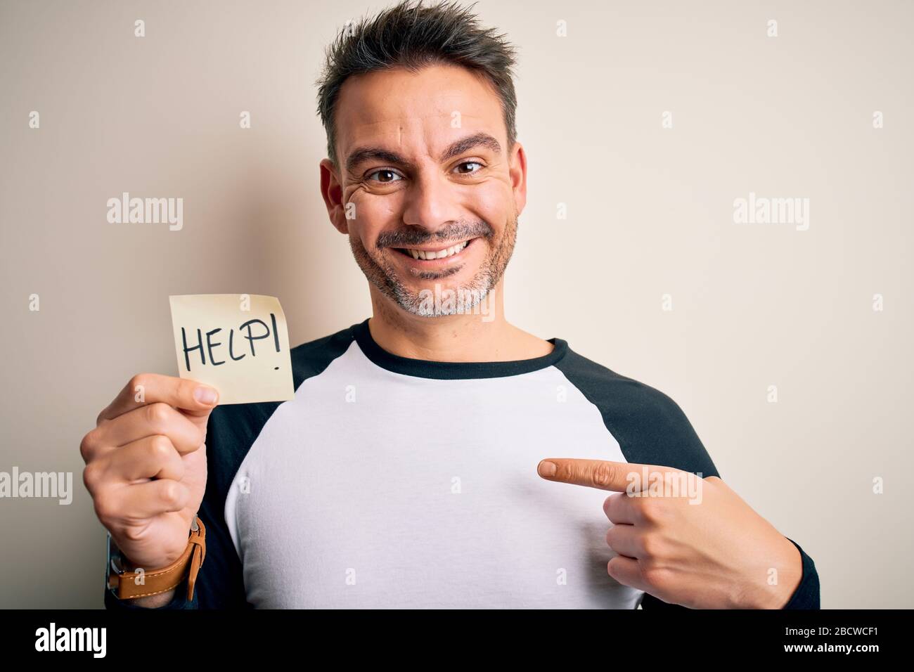Young handsome man stressed holding reminder paper with help message ...