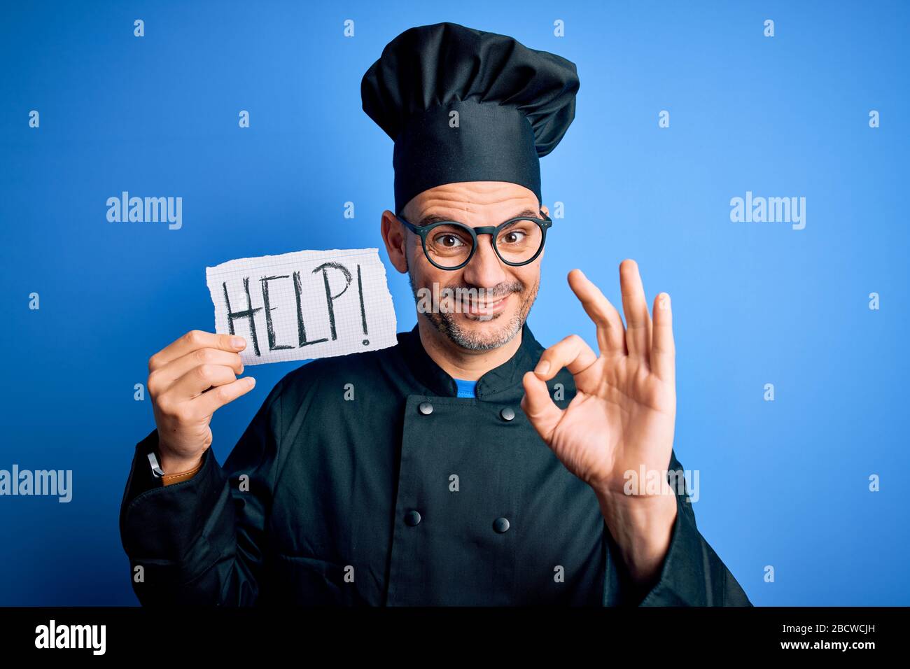 Young handsome chef man overworked wearing uniform and hat holding help ...