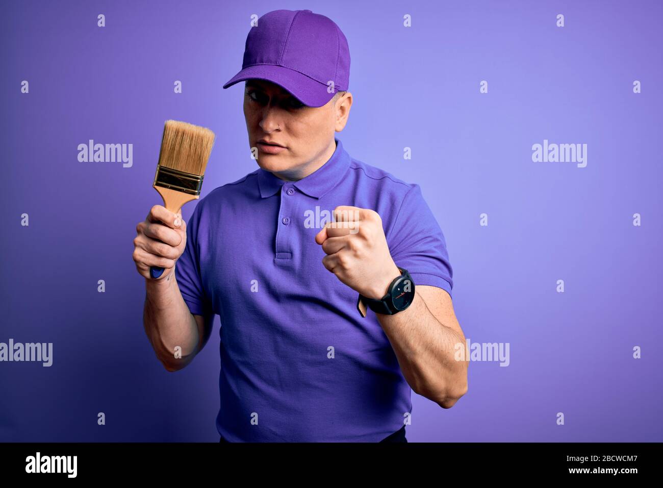 Young modern decorator painter man holding paint brush over purple ...