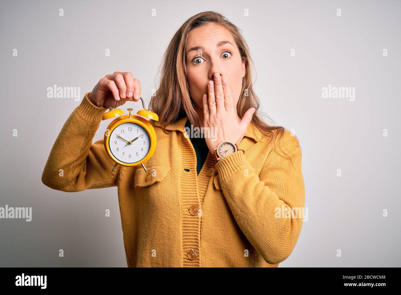 Young beautiful blonde woman holding alarm clock standing over isolated ...