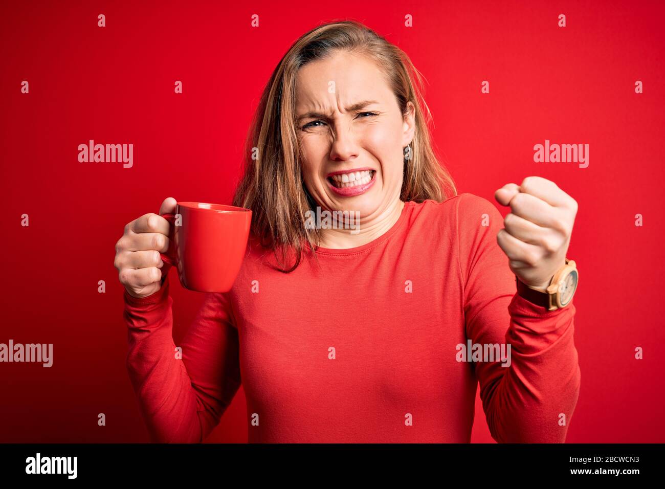 Young beautiful blonde woman drinking cup of coffee standing over ...