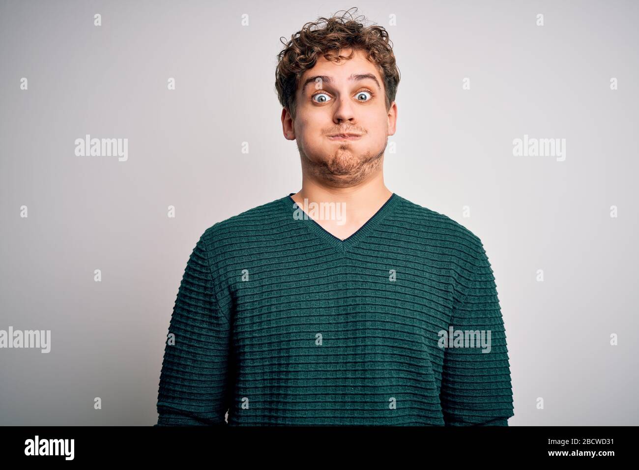 Young blond handsome man with curly hair wearing green sweater over ...