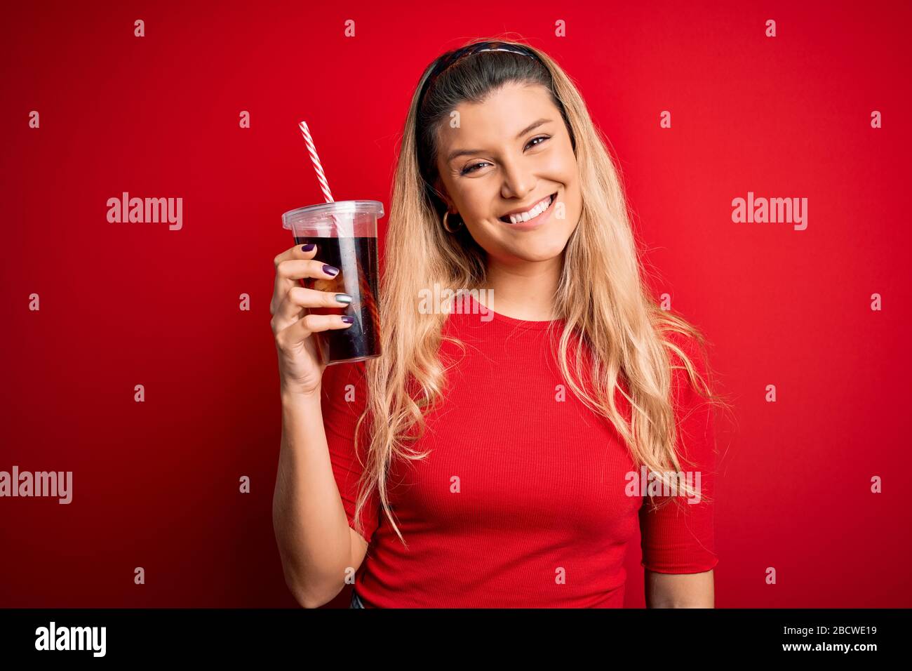 Young beautiful blonde woman drinking cola fizzy beverage using straw ...
