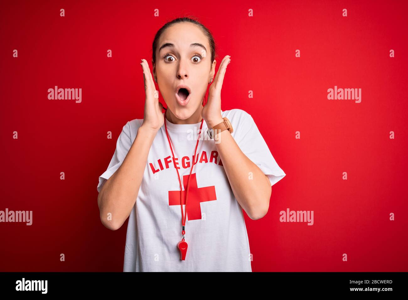 Beautiful lifeguard woman wearing t-shirt with red cross using whistle ...