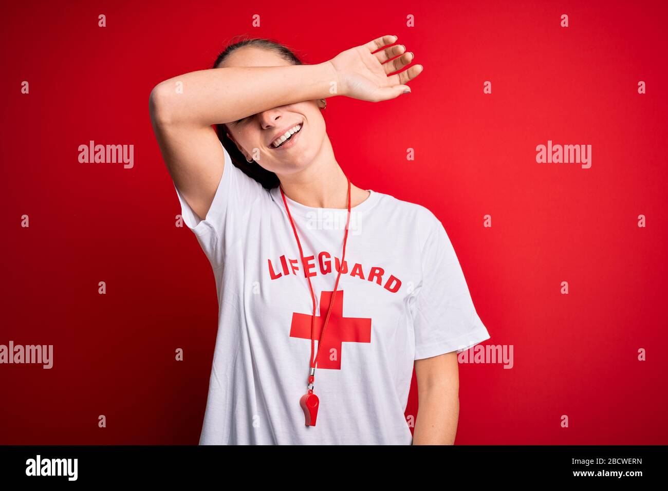 Beautiful lifeguard woman wearing t-shirt with red cross using whistle ...
