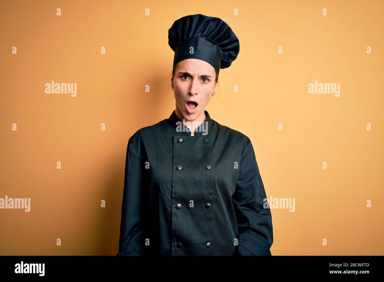 Young beautiful chef woman wearing cooker uniform and hat standing over ...