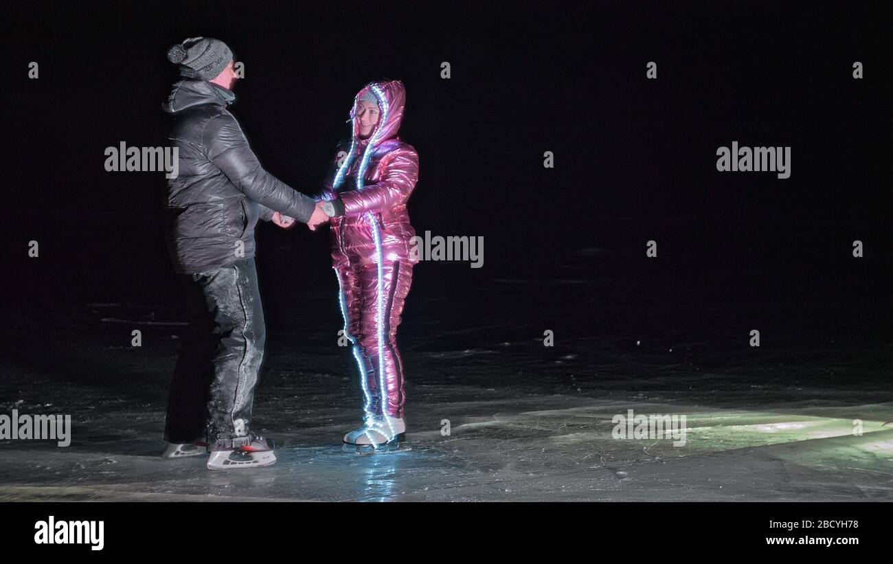 Young loving couple skating at ice rink at night. Man and woman kiss ...