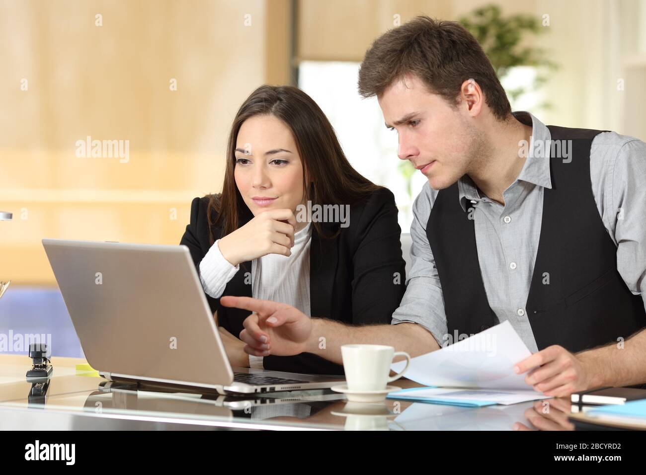 Two coworkers checking laptop content together and comparing documents ...