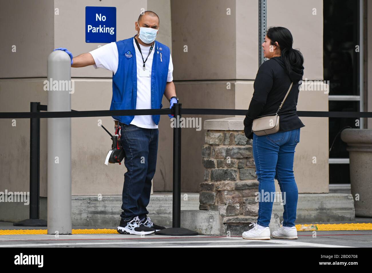 A Sam's Club employee wears a face mask and gloves while talking to a ...