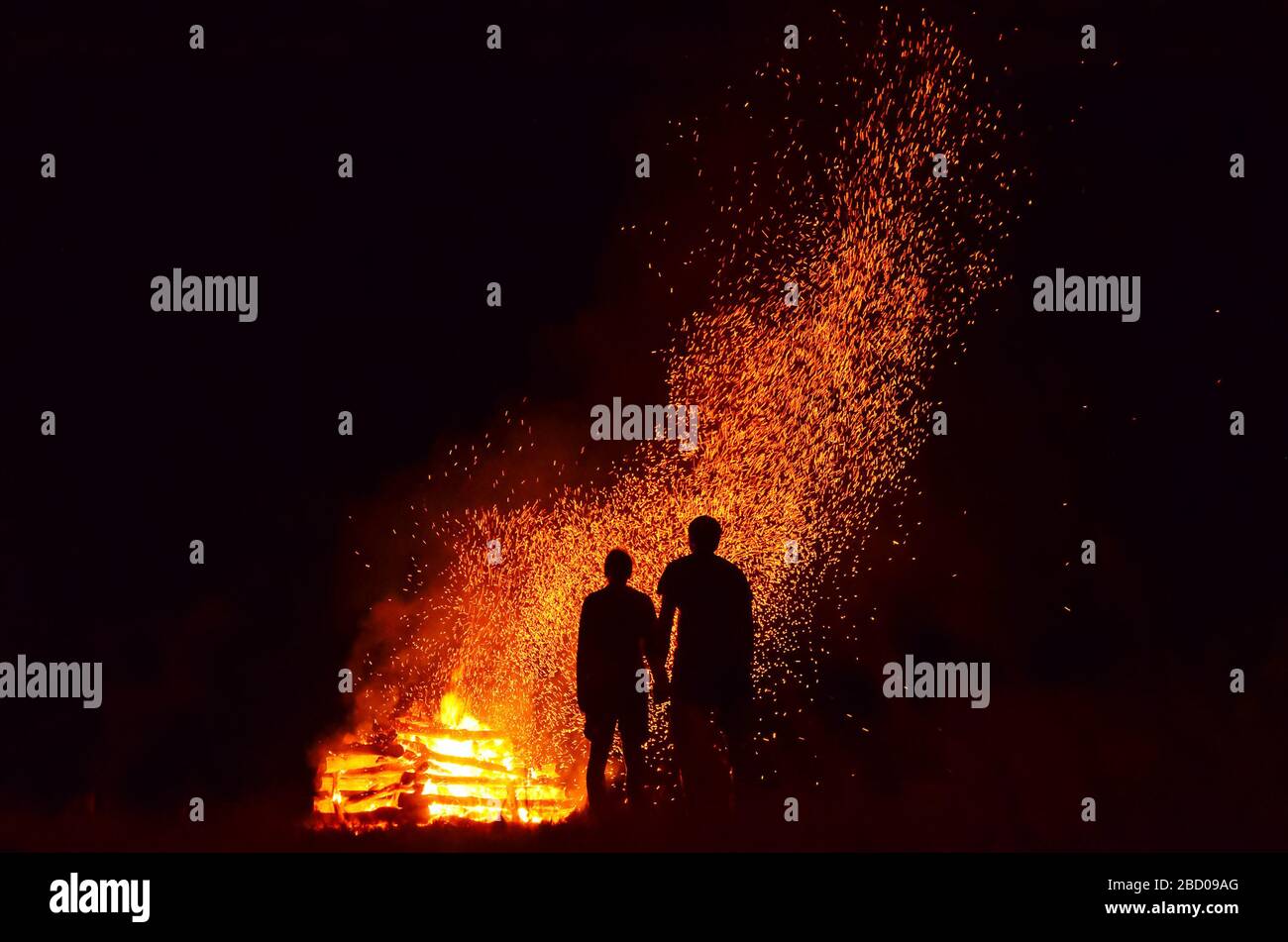 Young people in love standing together in front of big fire and looking ...