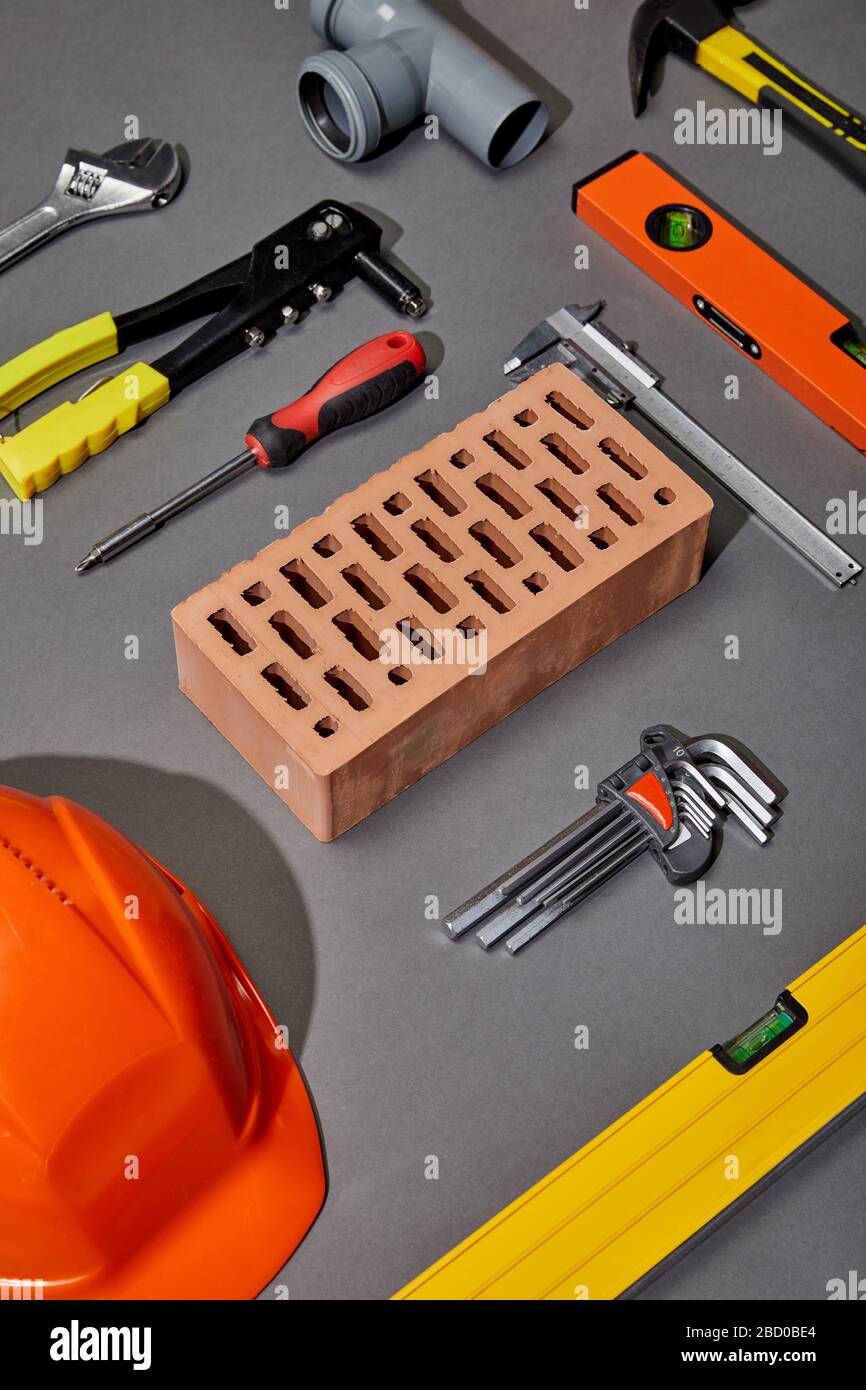 flat lay with orange helmet, brick, rivet gun, hammer, screwdriver ...