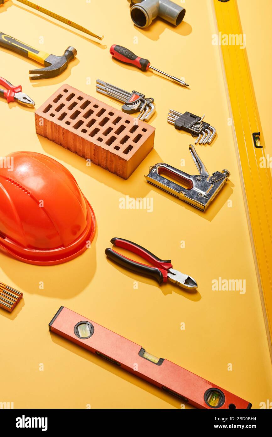 flat lay with industrial tools, brick and helmet on yellow background ...
